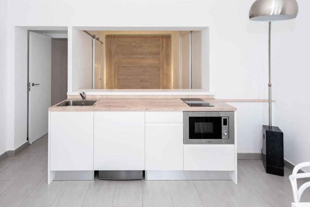 Cozinha moderna com micro-ondas embutido, pia e painel de parede em madeira.