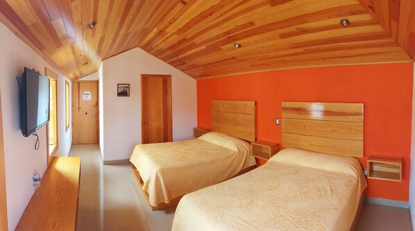 Quarto com duas camas, cabeceiras de madeira, uma televisão e teto de madeira.