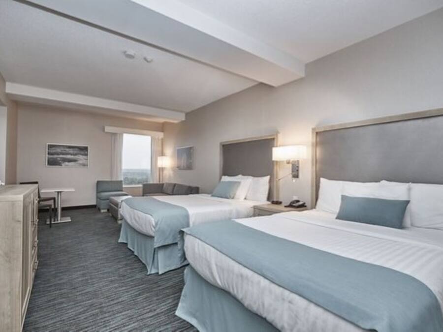 Quarto de hotel com duas camas, uma escrivaninha, uma cadeira e vista para o exterior.