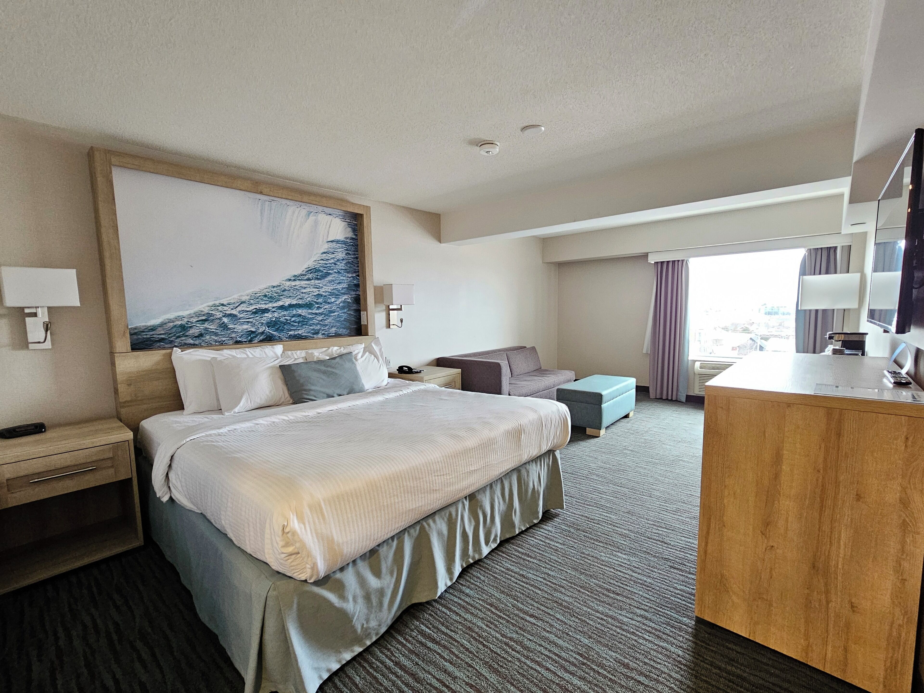 Quarto de hotel com uma cama grande, uma escrivaninha, uma cadeira, um sofá e um quadro grande na parede.