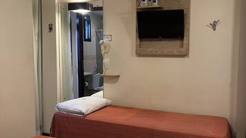 Quarto de hotel com duas camas de solteiro, televisão fixada na parede, um espelho e uma pequena estante com objetos decorativos.