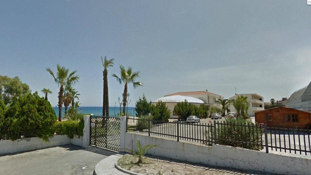 Uma área residencial costeira com portão fechado, palmeiras e vista para o mar.