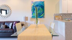 Uma sala de estar moderna com uma mesa de jantar de vidro, um sofá, um abajur e um quadro abstrato colorido.
