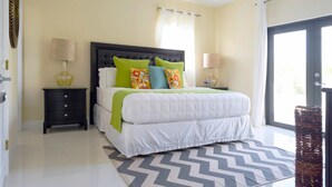 Quarto com uma cama grande, duas mesas de cabeceira, uma janela com cortinas e uma porta.