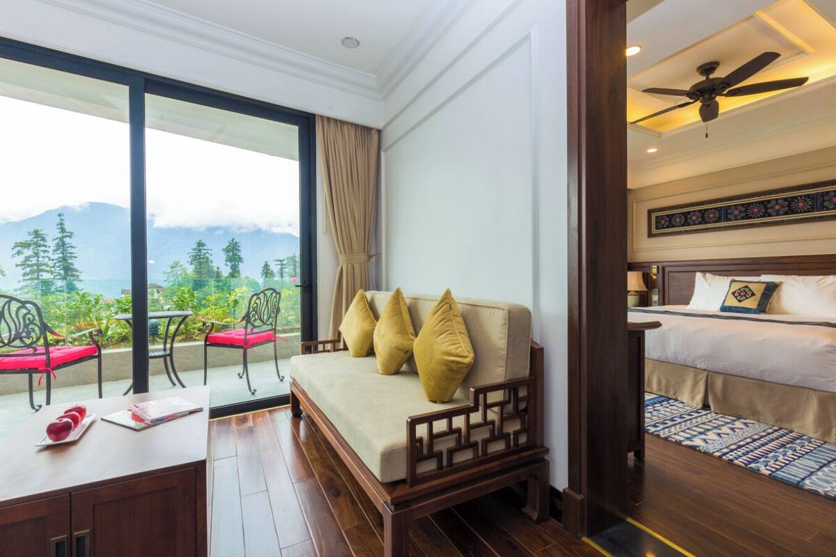 Quarto de hotel com sofá, cama, escrivaninha e vista para as montanhas.