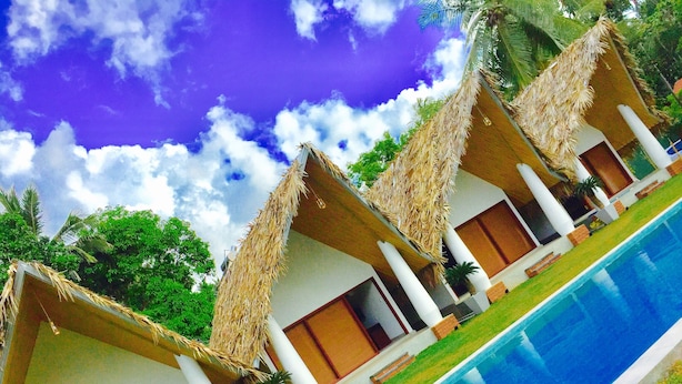 Vista da piscina de um resort com cabanas de telhado de palha e uma piscina azul cristalina.