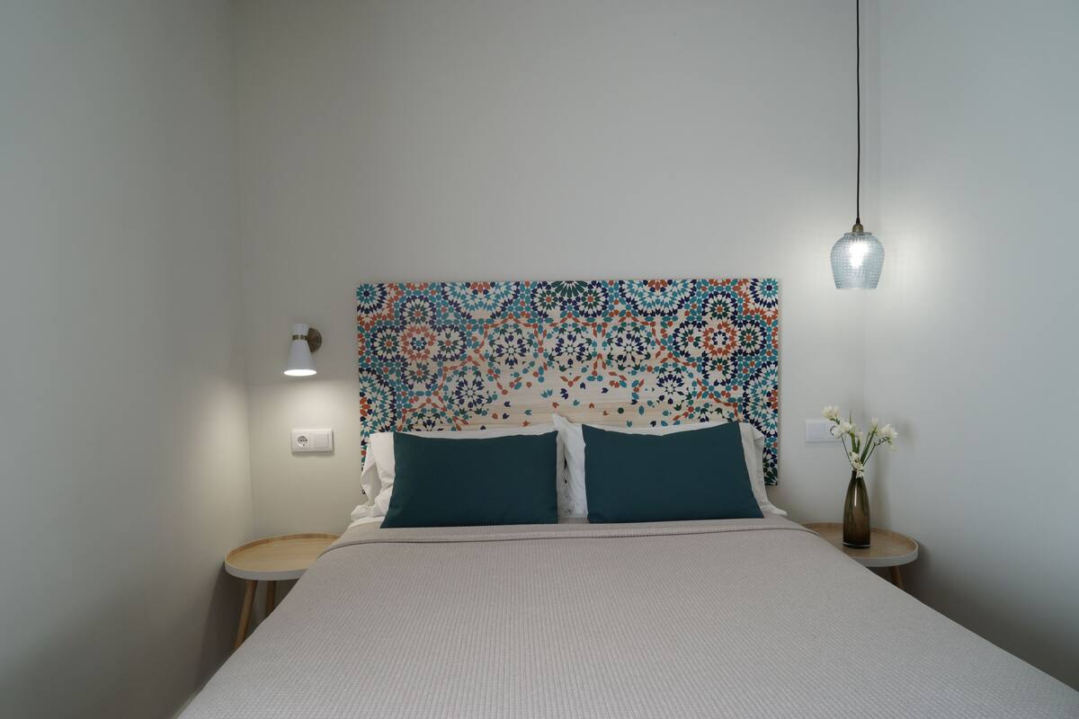 Quarto bem arrumado com cabeceira estampada, mesa de cabeceira com um vaso e luminária pendente.