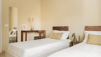 Quarto de hotel com duas camas, uma mesa pequena com cadeira, mesa de cabeceira com abajur e um espelho.