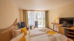 Quarto de hotel com duas camas, televisão, secretária com abajur, uma cadeira e vista para o exterior.