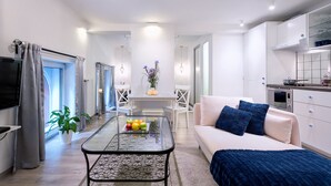 Uma sala de estar moderna com um sofá, uma mesa de centro com frutas, uma televisão e uma área de cozinha com armários e um micro-ondas.