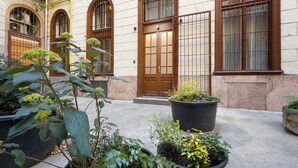 Um edifício com janelas em arco e uma porta central, rodeado por plantas em vasos.