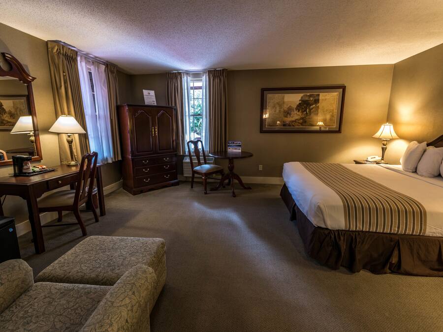 Quarto de hotel com cama, escrivaninha, cadeira, cômoda e janela com cortinas.