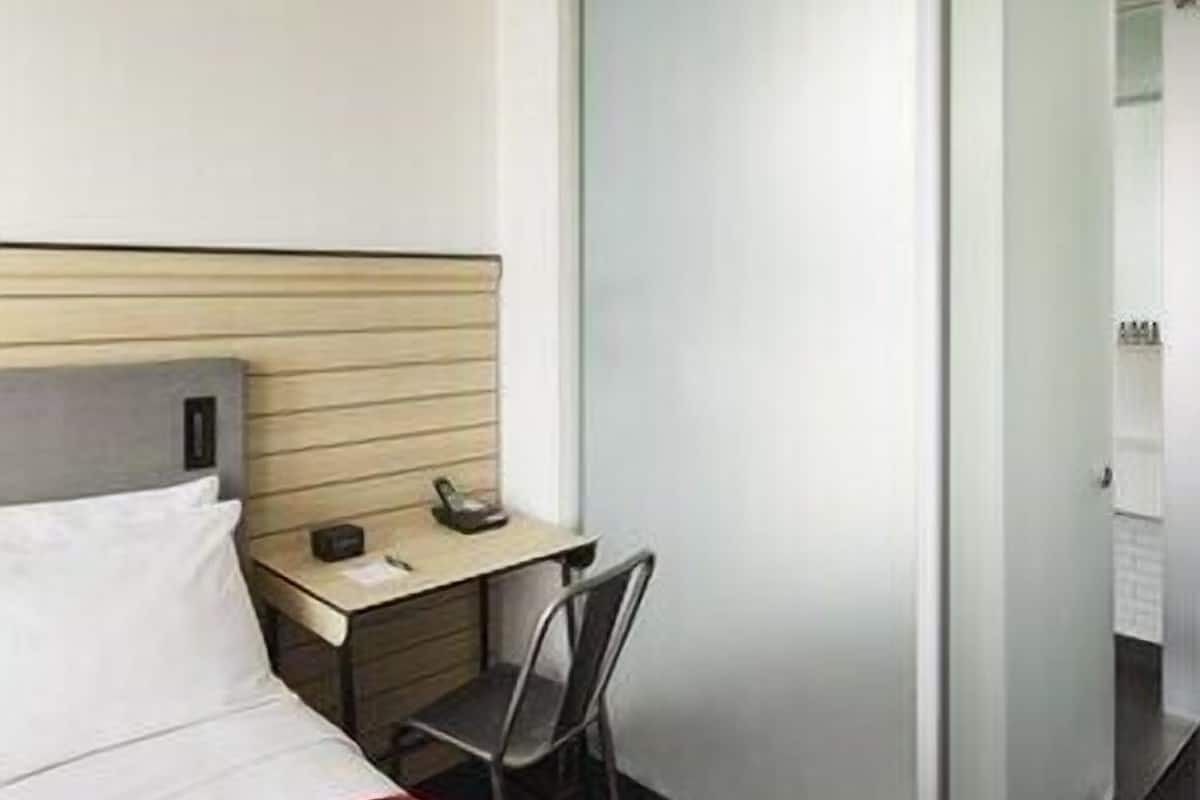 Quarto de hotel com cama, escrivaninha, cadeira e porta deslizante.