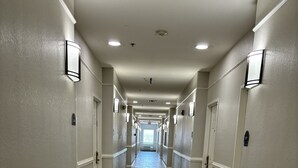 Um corredor comprido e estreito, com paredes em tons claros e soalho de madeira, que termina numa porta.