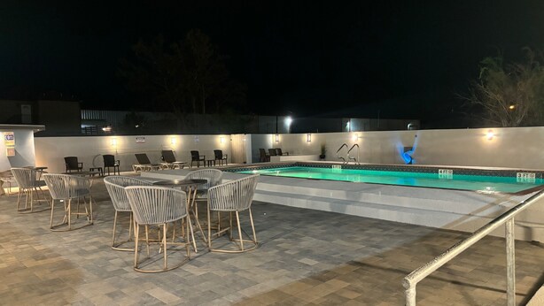 Uma área de piscina ao ar livre com espreguiçadeiras e mesas, um deck ladrilhado e uma piscina com iluminação azul.