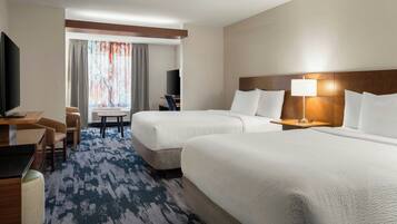 Quarto de hotel com duas camas, uma mesa, uma TV e uma janela com cortinas.