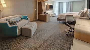 Quarto de hotel com sofá, cama, escrivaninha e televisão.