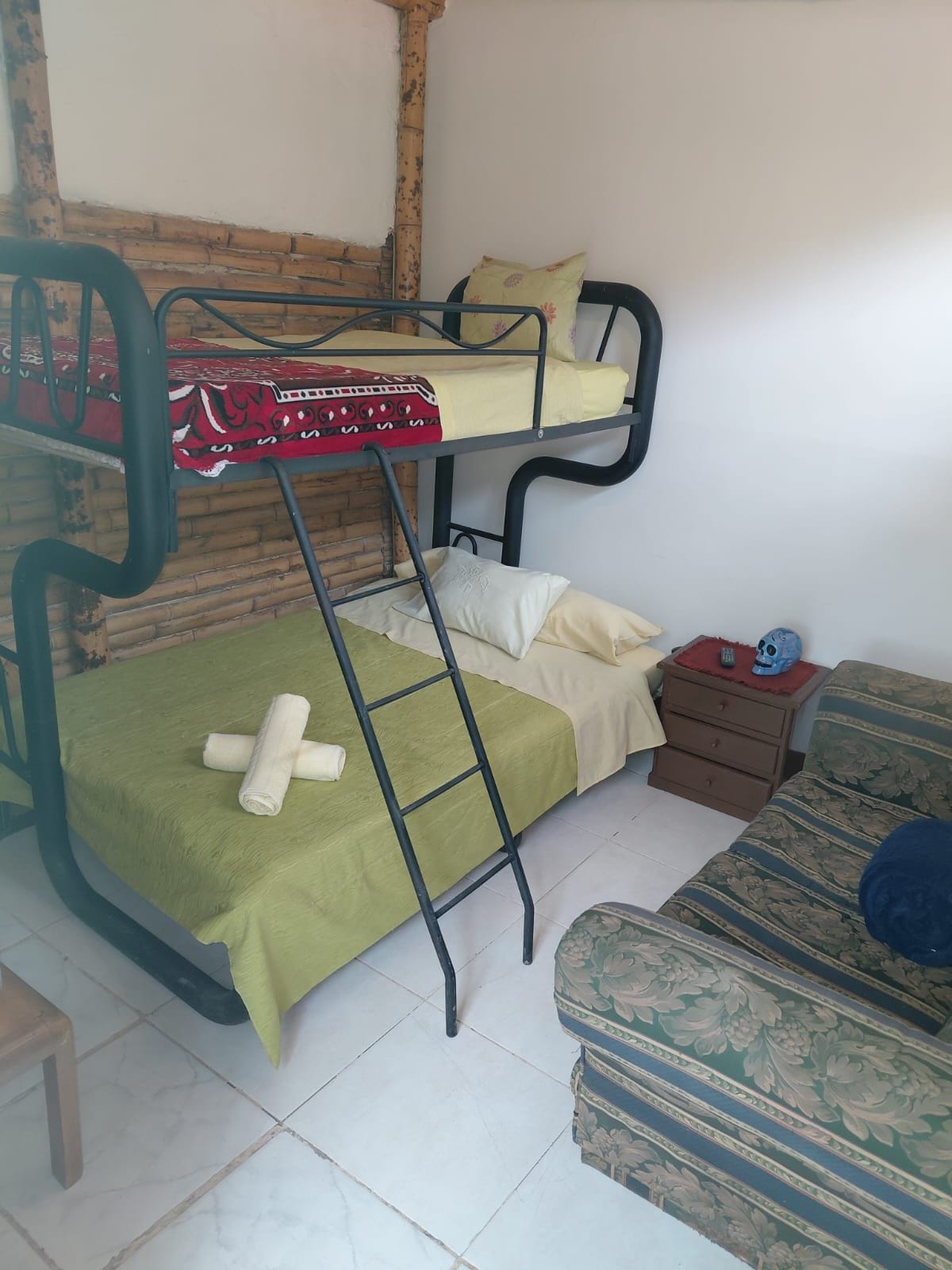 Um dormitório com beliches, uma mesinha com uma decoração de caveira e um sofá estampado.