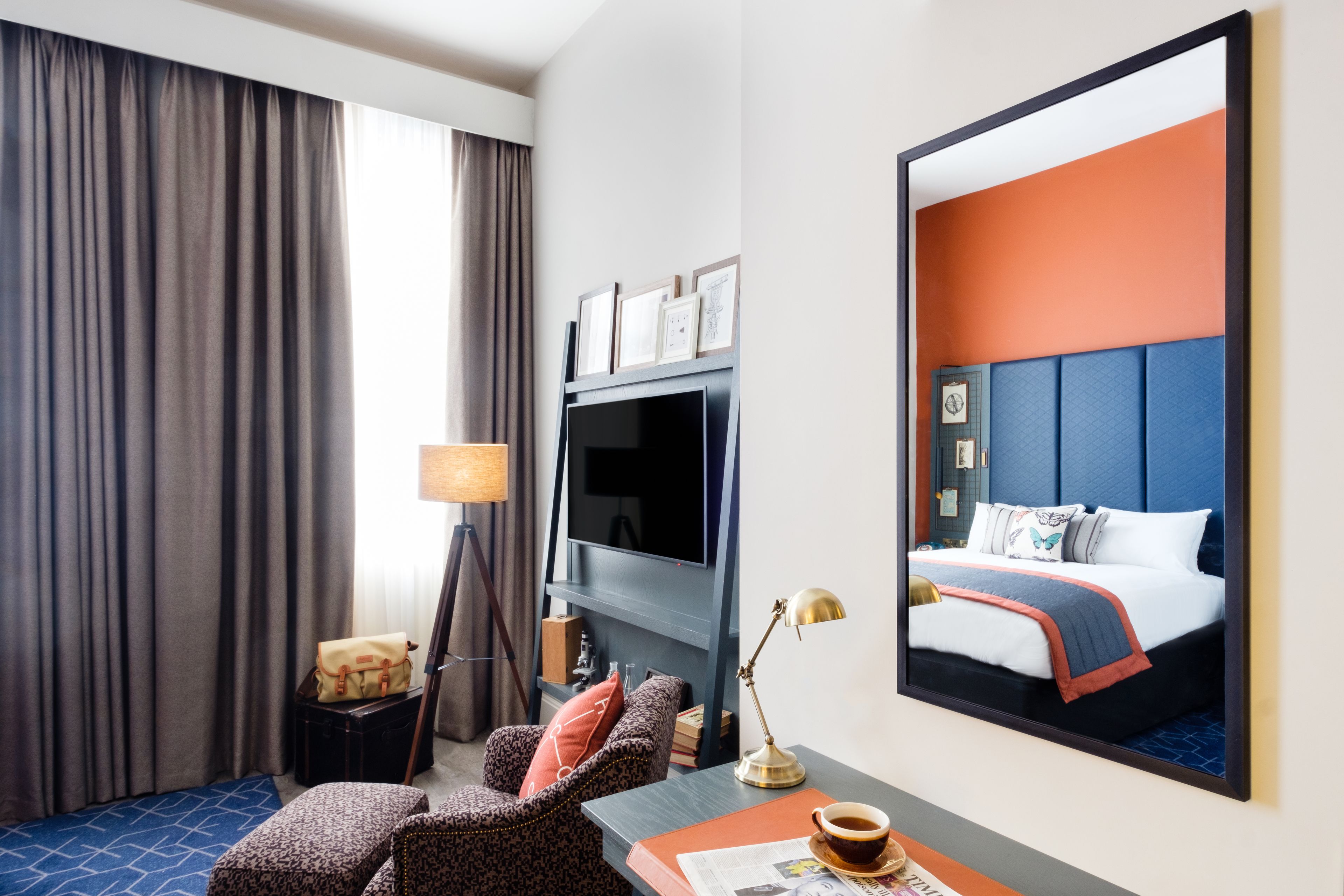 Quarto de hotel com uma cama grande, televisão de tela plana, escrivaninha com luminária, uma cadeira e vista para a cidade pela janela.