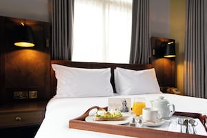 Quarto de hotel com cama bem arrumada, bandeja com itens de café da manhã e um cartão.