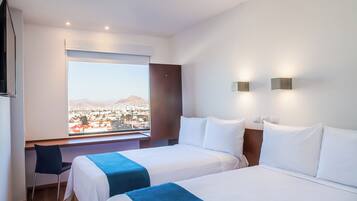 Quarto de hotel com duas camas, uma escrivaninha e uma grande janela com vista para a cidade.
