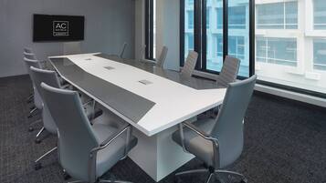 Uma sala de conferências com uma mesa comprida, seis cadeiras, uma TV de tela plana e janelas amplas.