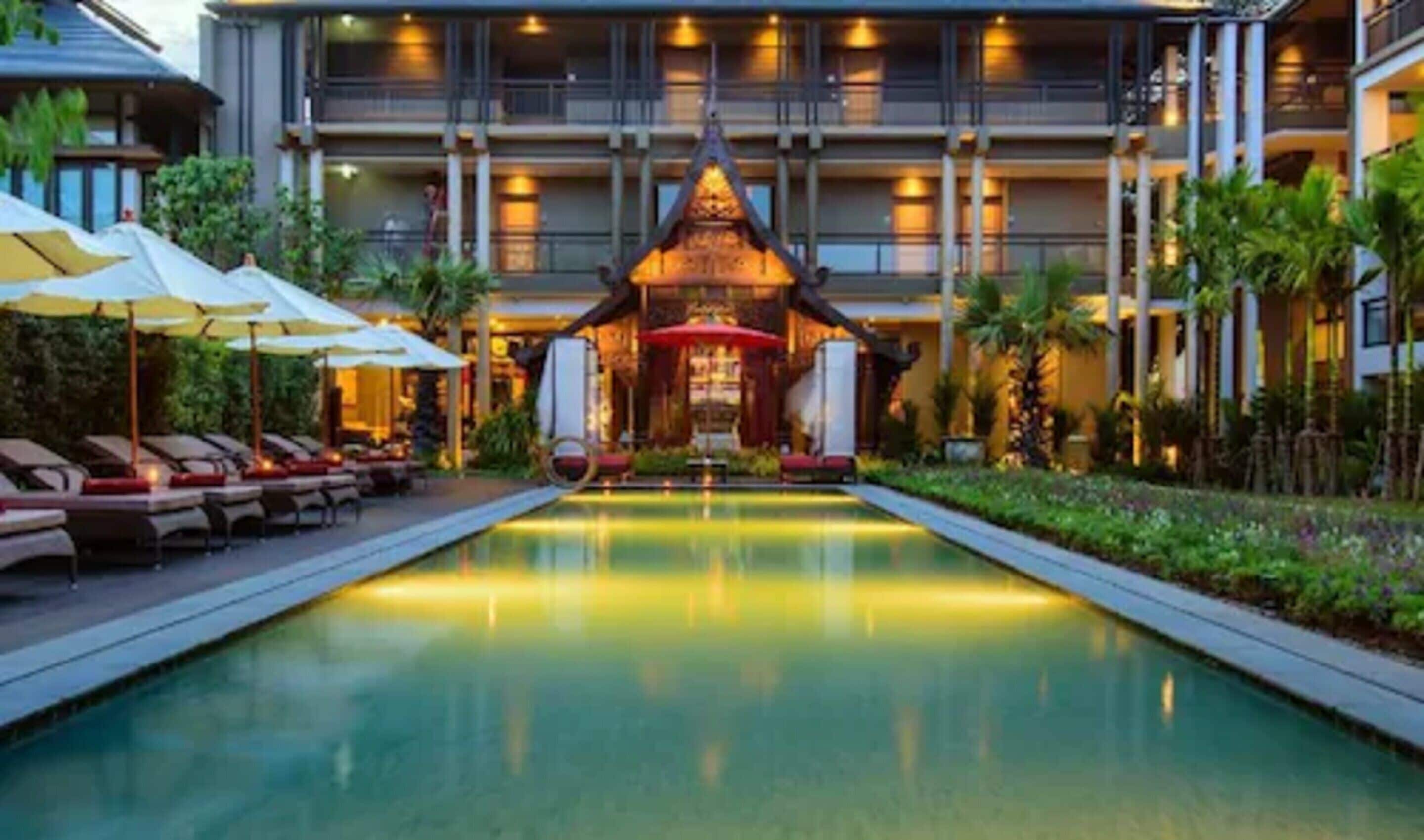 Um hotel com piscina, espreguiçadeiras e uma estrutura tradicional tailandesa no centro.