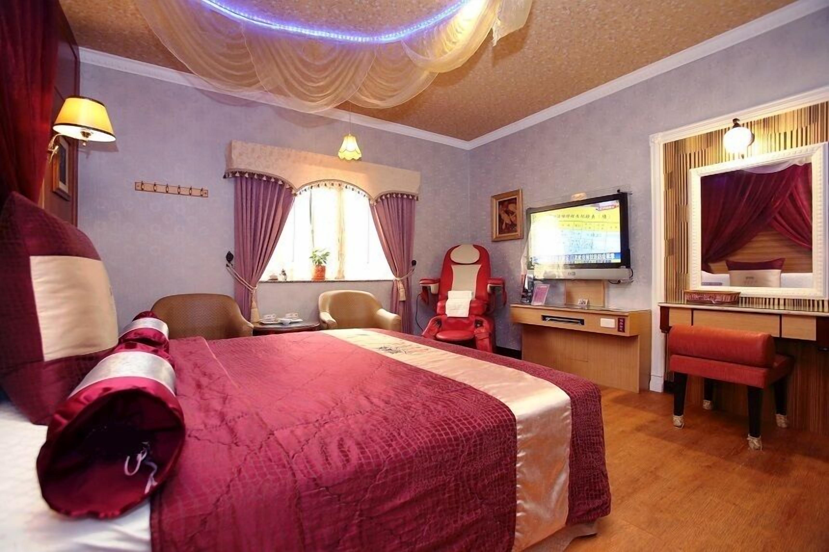 Quarto de hotel com cama, escrivaninha, cadeira, televisão e espelho.