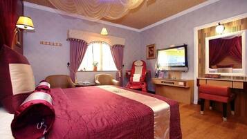 Quarto de hotel com cama, escrivaninha, cadeira, televisão e espelho.