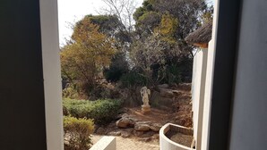 Um caminho de pedra leva a um jardim com uma estátua, cercado por árvores e um muro de pedra.