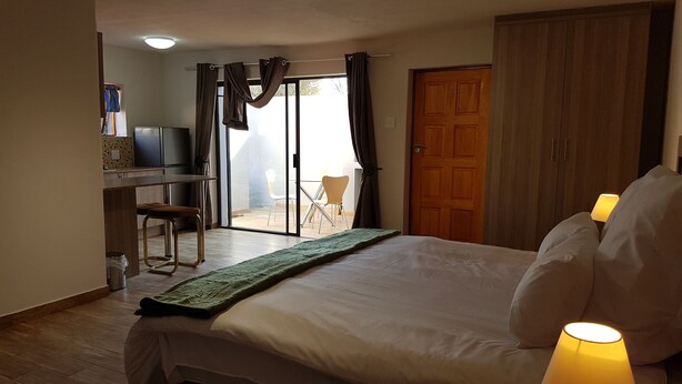Quarto com cama, escrivaninha com cadeira, televisão e porta de vidro que dá para uma área externa.