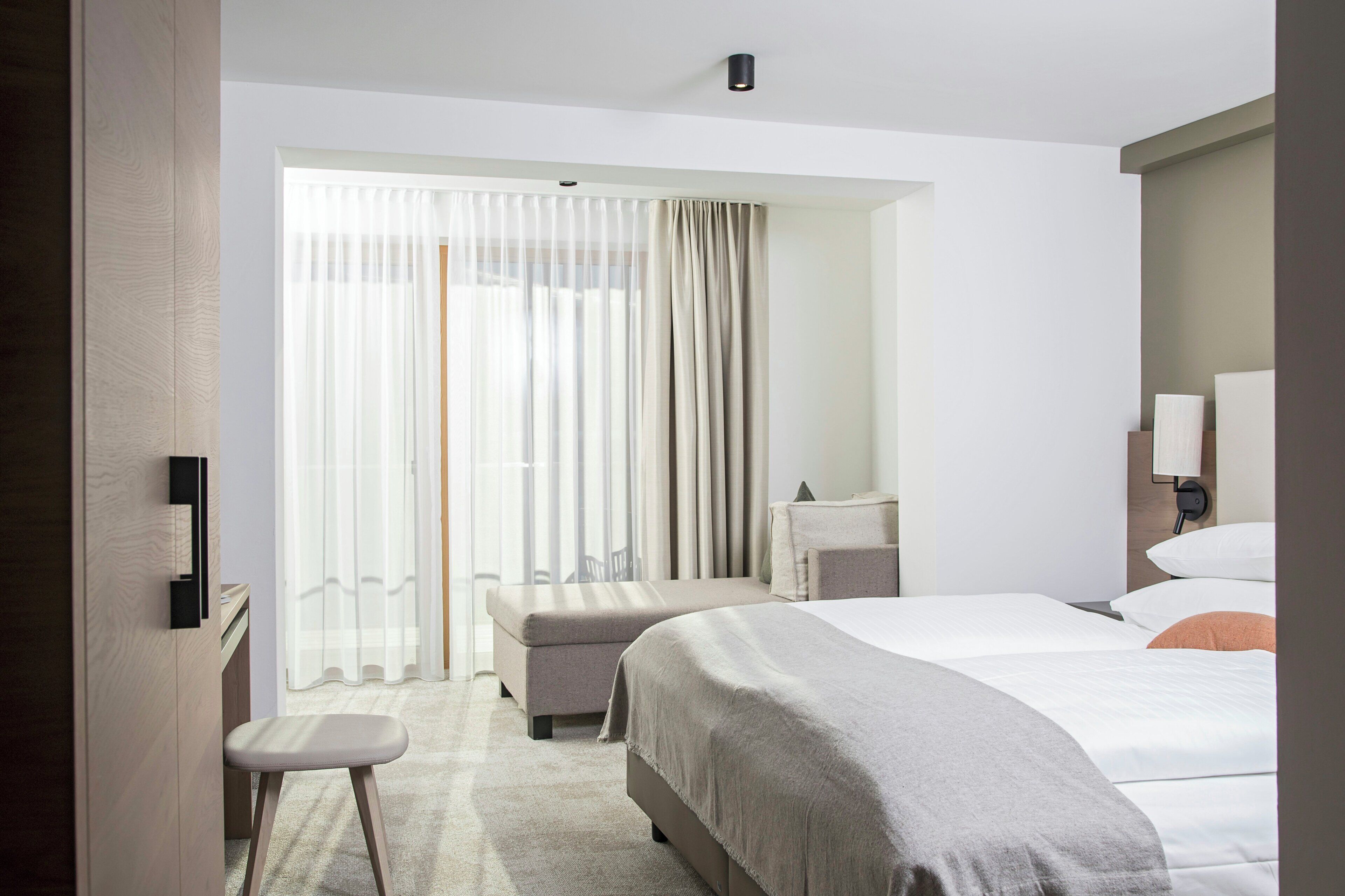 Quarto de hotel com cama, área de estar, escrivaninha e janela com cortinas.