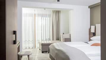 Quarto de hotel com cama, área de estar, escrivaninha e janela com cortinas.