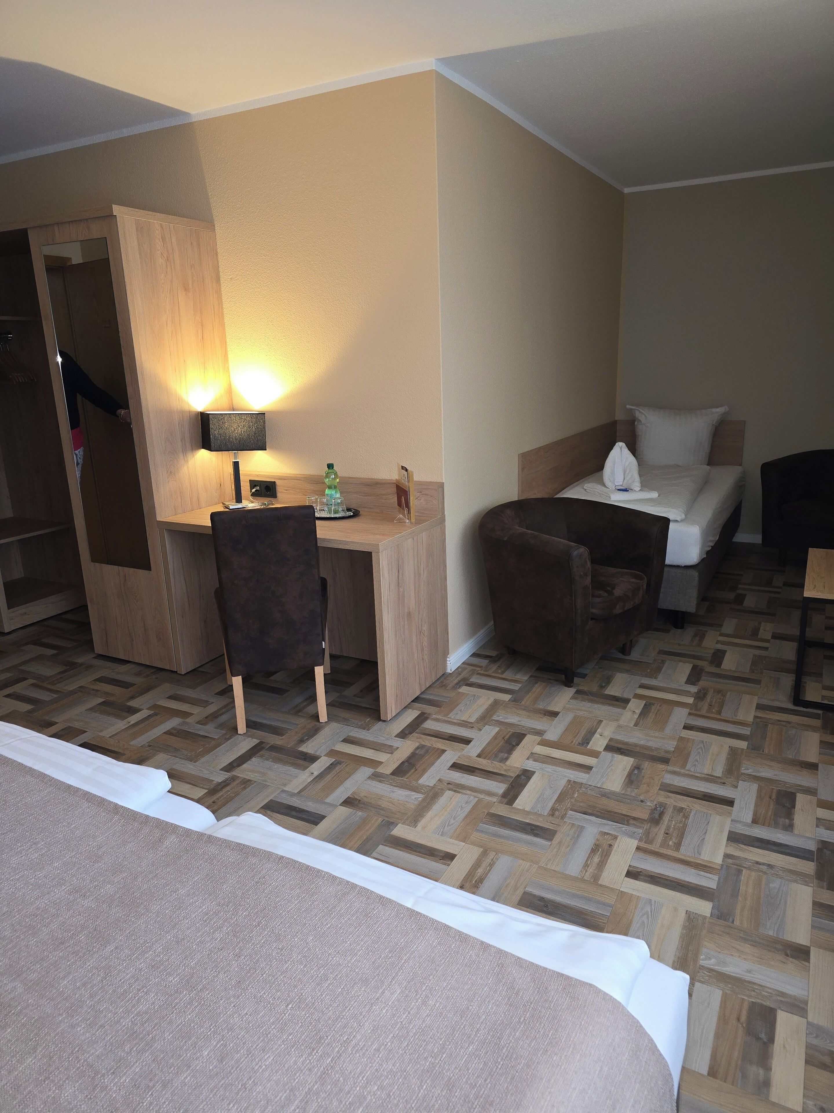 Quarto de hotel com cama, escrivaninha, cadeira, mesinha de centro e guarda-roupa.