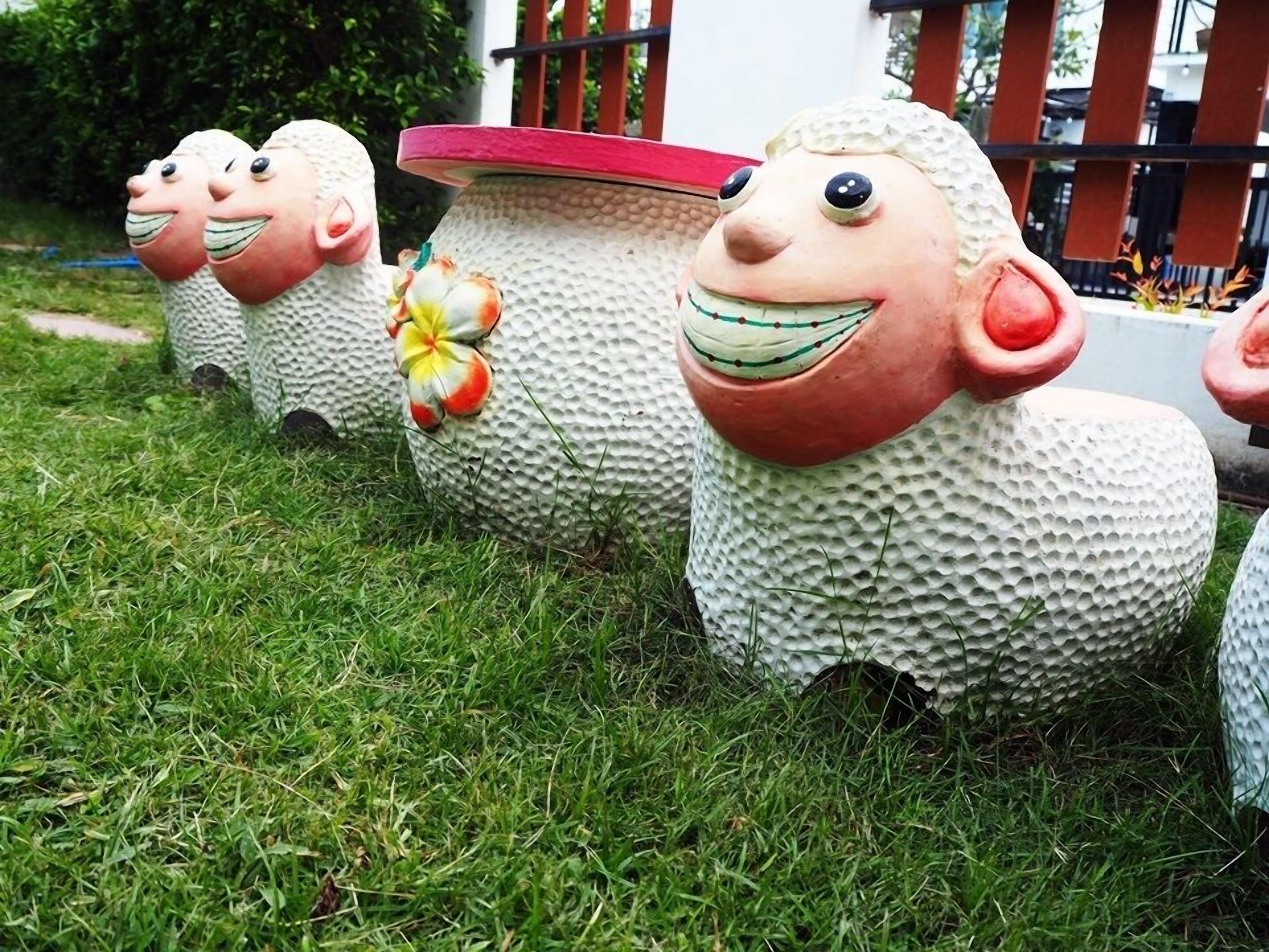 Fileira de esculturas em formato de ovelha, com superfícies texturizadas e detalhes coloridos, dispostas sobre a grama.