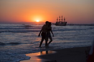 Um pôr do sol sobre o oceano com um navio ao fundo.