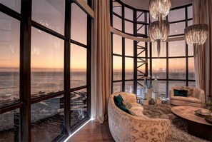 Uma sala de estar moderna com amplas janelas do chão ao teto, uma escadaria em curva e vista para o oceano.