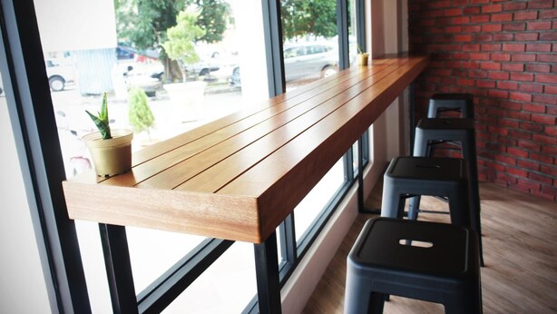 Um banco de madeira com uma planta em vaso, banquetas pretas e uma parede de tijolos.