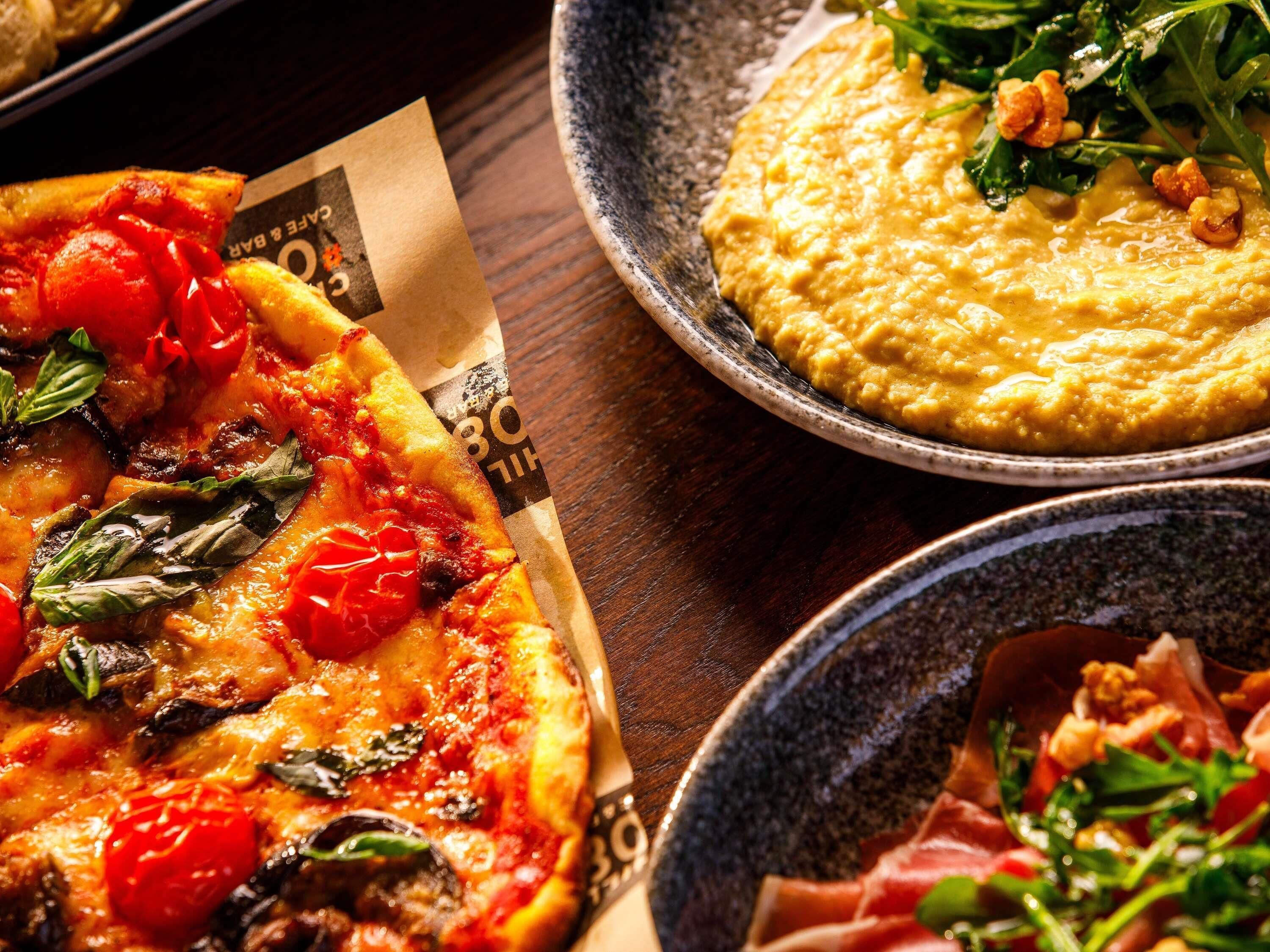 Pizza com cobertura, um prato de homus e presunto com folhas.