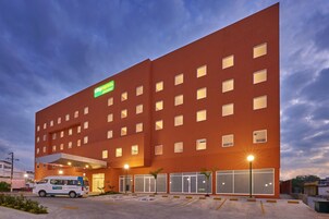 Um hotel de vários andares com fachada vermelha, várias janelas e um estacionamento com uma van.