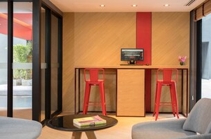 Quarto moderno com parede de destaque em madeira, TV de tela plana, dois banquetes vermelhos e uma mesa redonda com um livro.