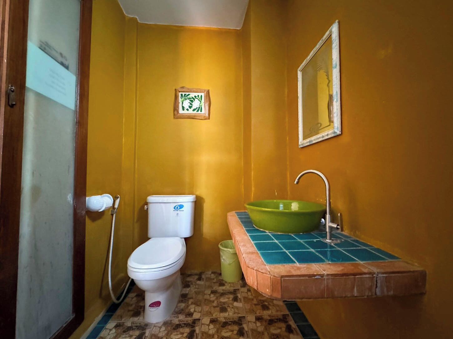 Casa de banho com sanita, lavatório verde e espelho pequeno.