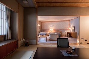Quarto de hotel com estética japonesa tradicional, apresentando tatames, uma mesa de madeira baixa e uma cama com cabeceira.