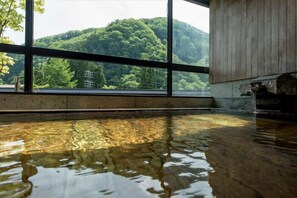 Quarto com uma grande janela com vista para uma colina arborizada, um banco de madeira e um pequeno elemento aquático.