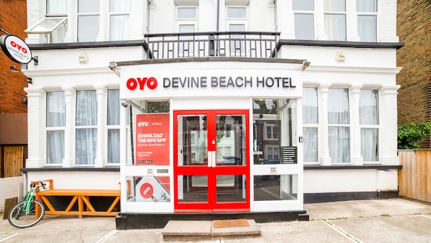 Exterior do Hotel Devine Beach, com uma porta vermelha chamativa e um aviso publicando o aplicativo OYO.