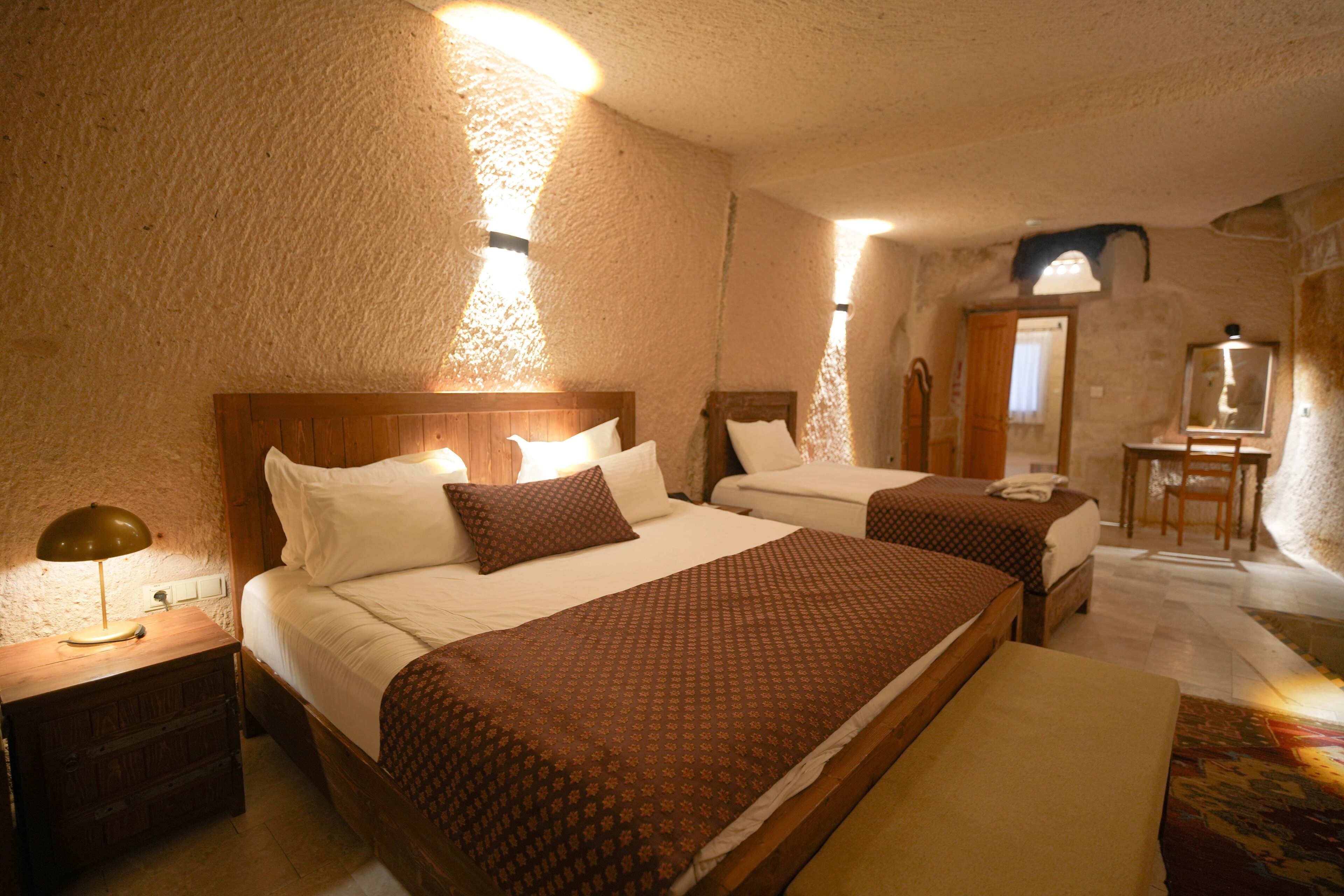 Quarto de hotel com duas camas, uma cabeceira de madeira, uma mesa de cabeceira, uma escrivaninha e uma cadeira.