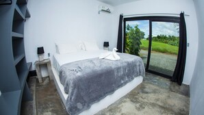 Quarto com cama, mesa de cabeceira, ar condicionado fixado na parede e vista através de uma porta de vidro.