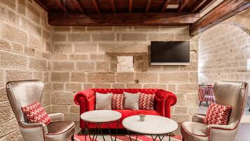 Um quarto aconchegante com um sofá vermelho, duas poltronas e uma TV fixada na parede.