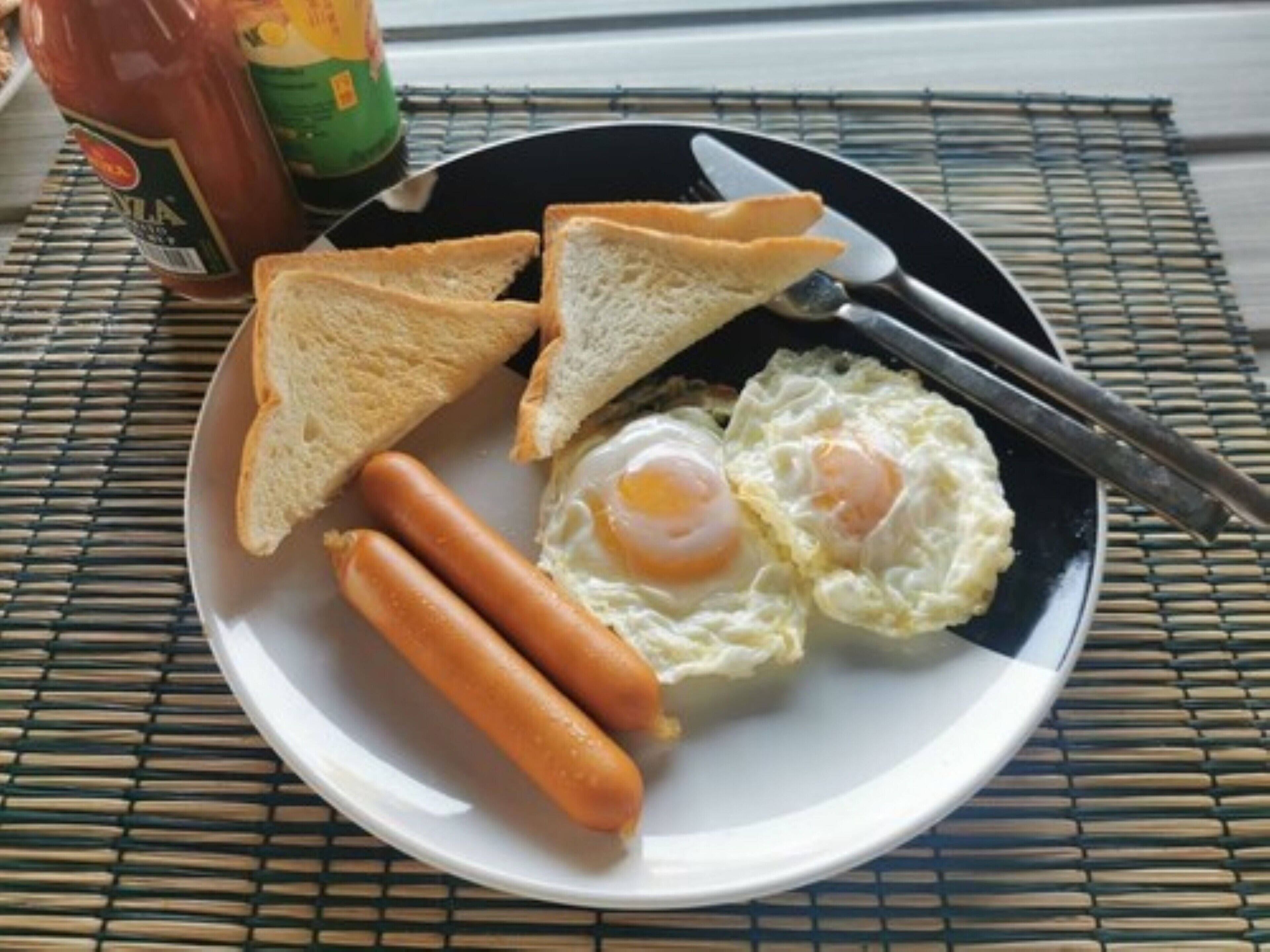 Um prato com dois ovos fritos, duas fatias de torrada e uma salsicha.