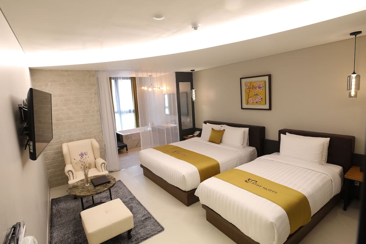 Quarto de hotel com duas camas, um sofá, uma televisão, uma escrivaninha e um banheiro.